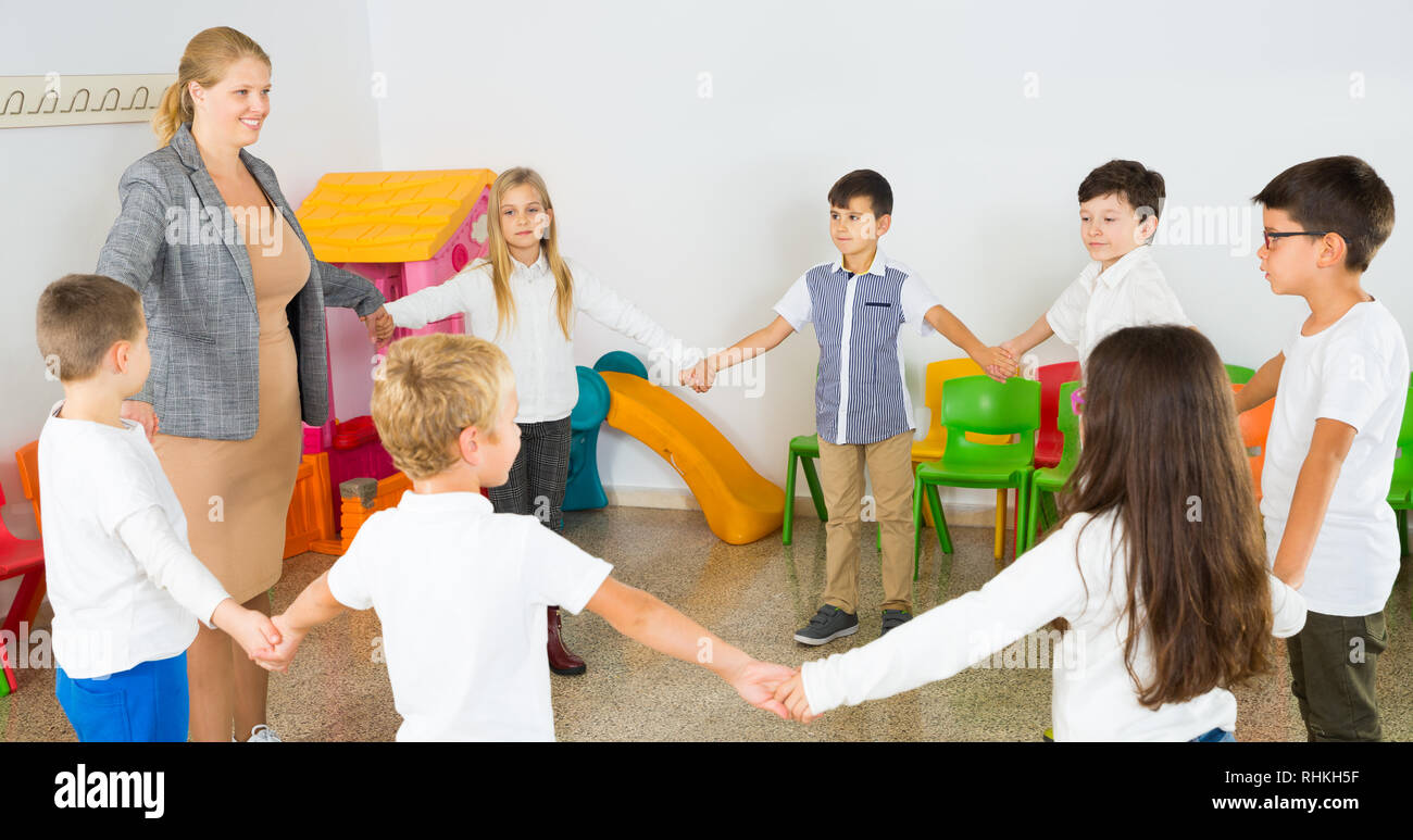Group of happy children standing in circle holding hands, playing with their teacher in ...