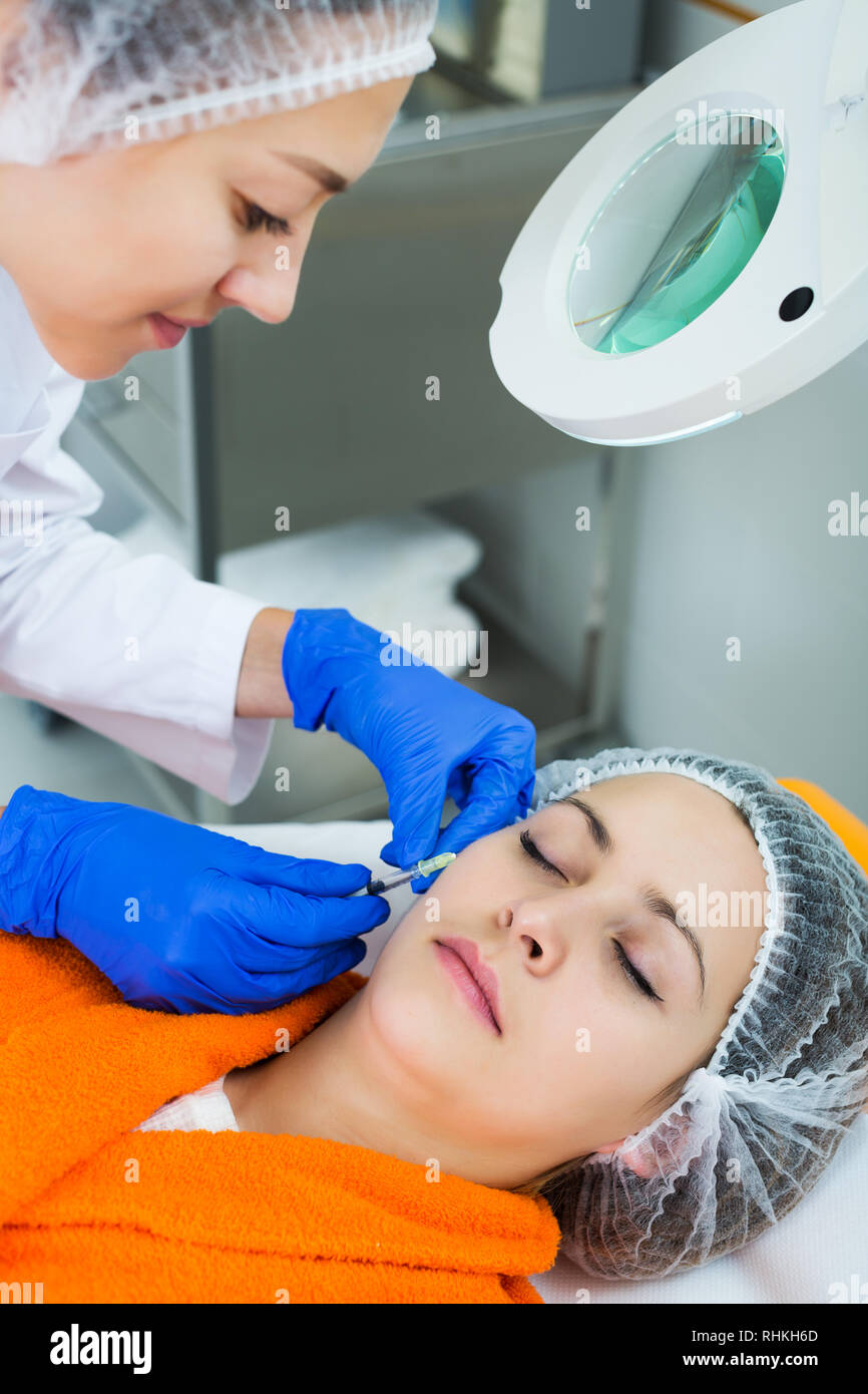 Positive young doctor using injection in beauty procedures to woman ...