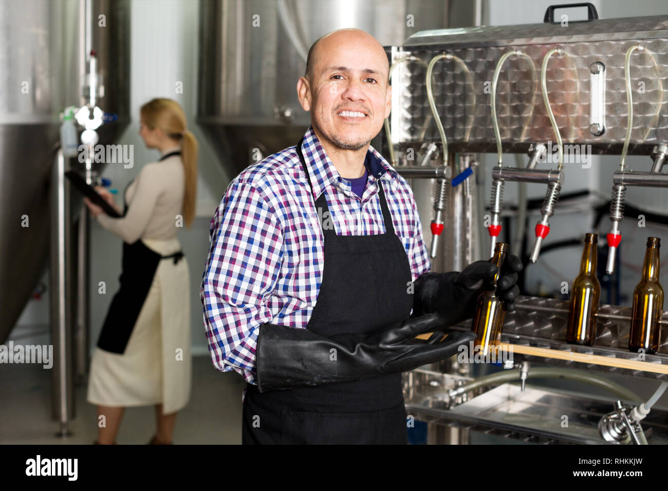 Cheerful man employee bottling beer in glass bottles on modern facility ...