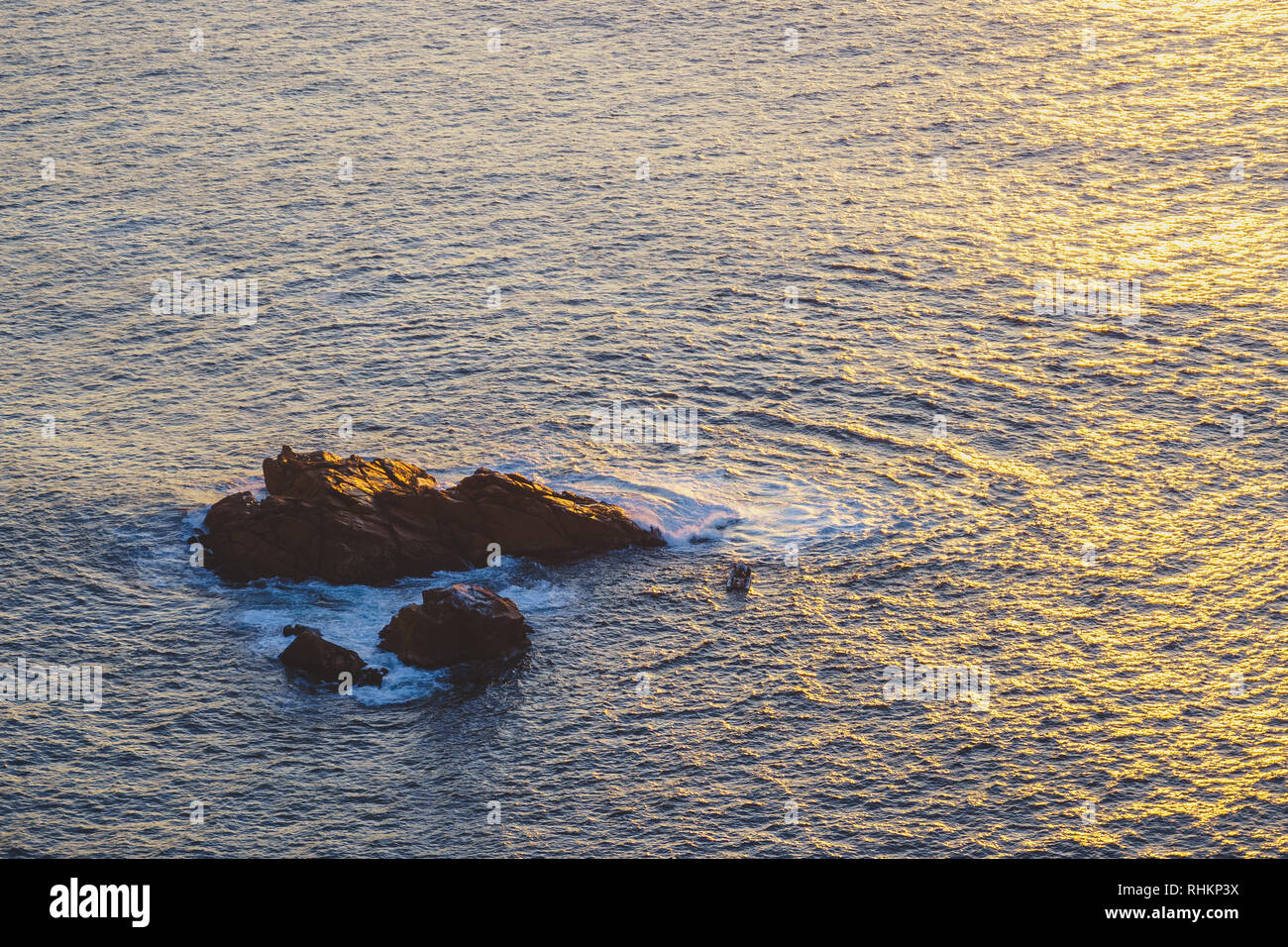 Small tiny boat with breaking waves close to a small rock island at ...