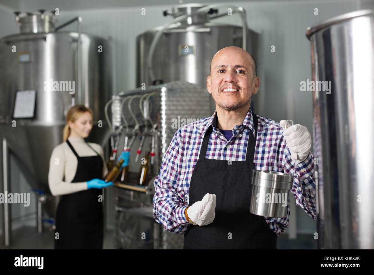 Mature cheerful man wearing the uniform standing among the brewery ...