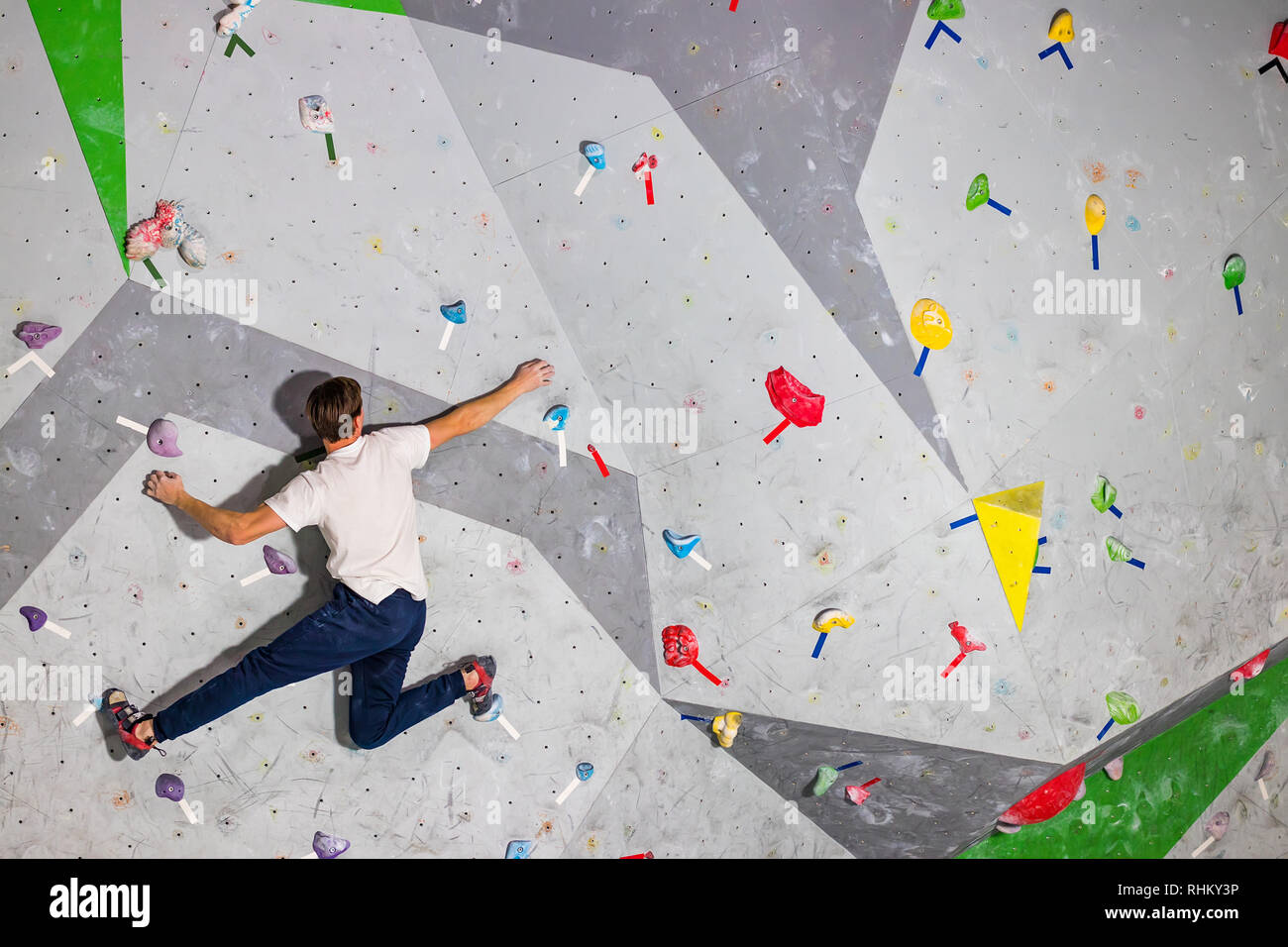 Rock climber man hanging on a bouldering climbing wall, inside on ...