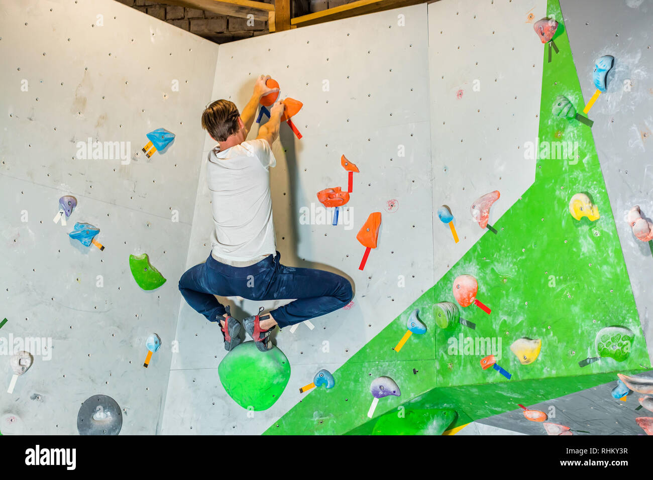Rock climber man hanging on a bouldering climbing wall, inside on ...