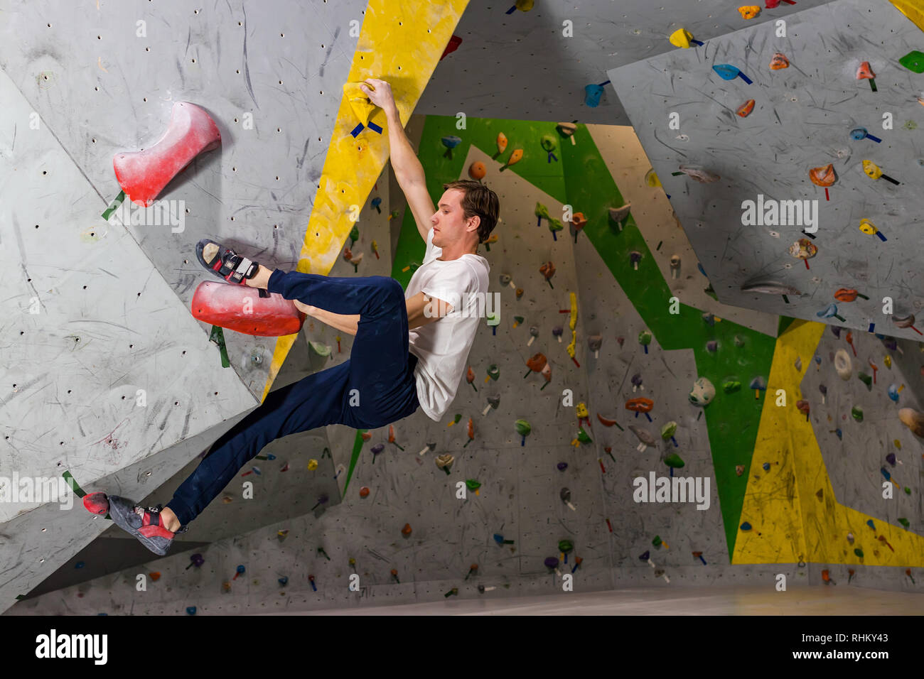 Rock climber man hanging on a bouldering climbing wall, inside on ...