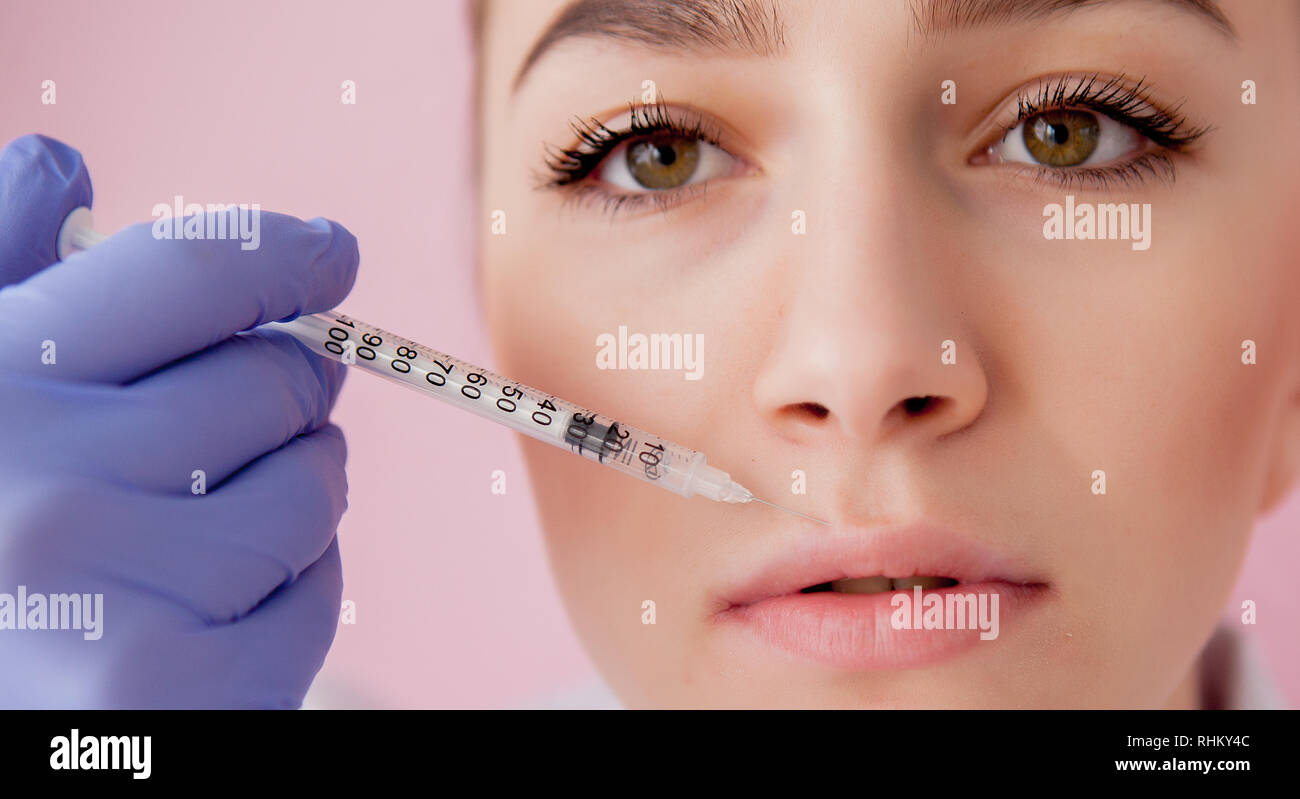 Doctor in gloves giving woman botox injections in lips, on pink ...