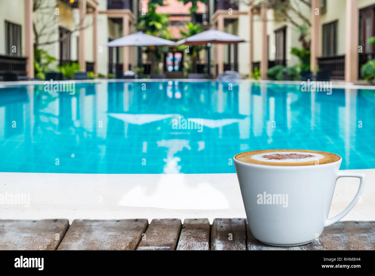A white cup of coffee on the wooden table by the pool Stock Photo - Alamy