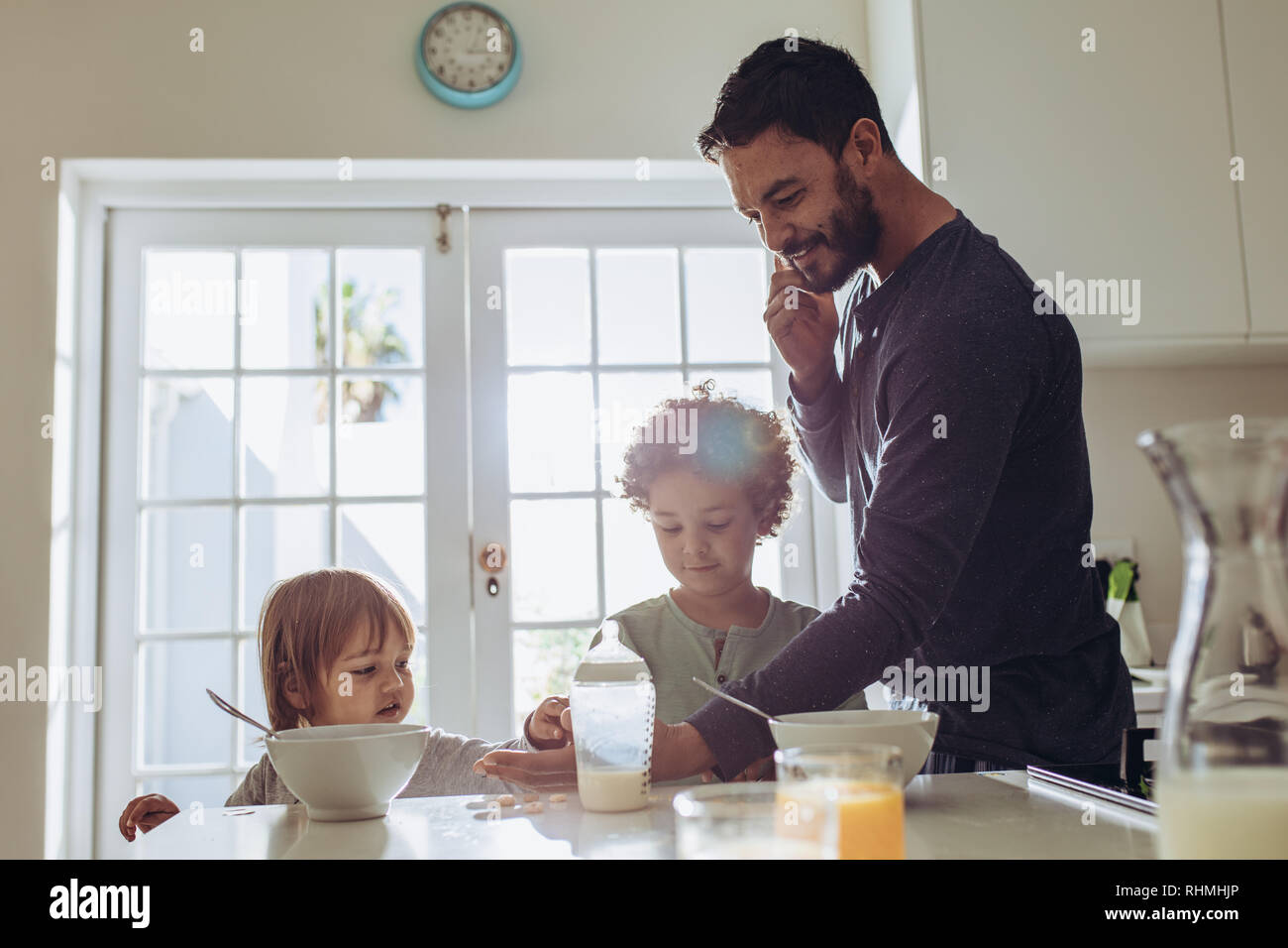 Man standing at the breakfast table talking over mobile phone with kids ...