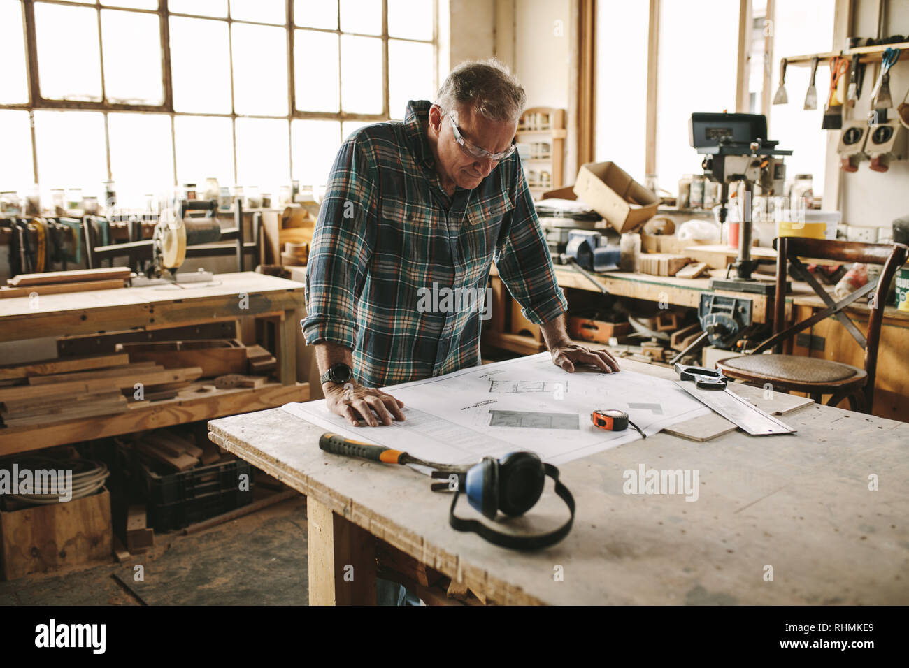 Senior carpenter studying drawing before starting his work at workshop ...