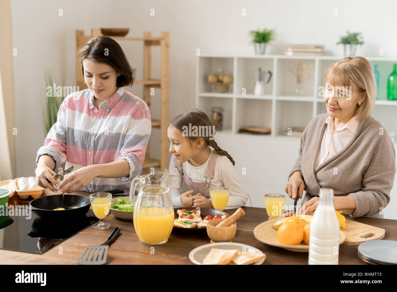 Young woman breaking egg over hot frying pan while cooking breakfast ...
