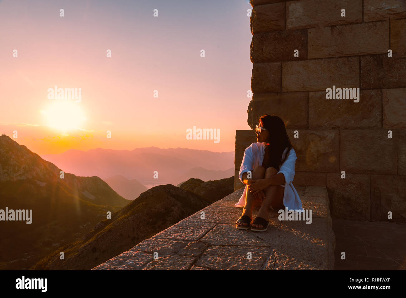 woman siting at the edge with beautiful view of sunset over mountains ...