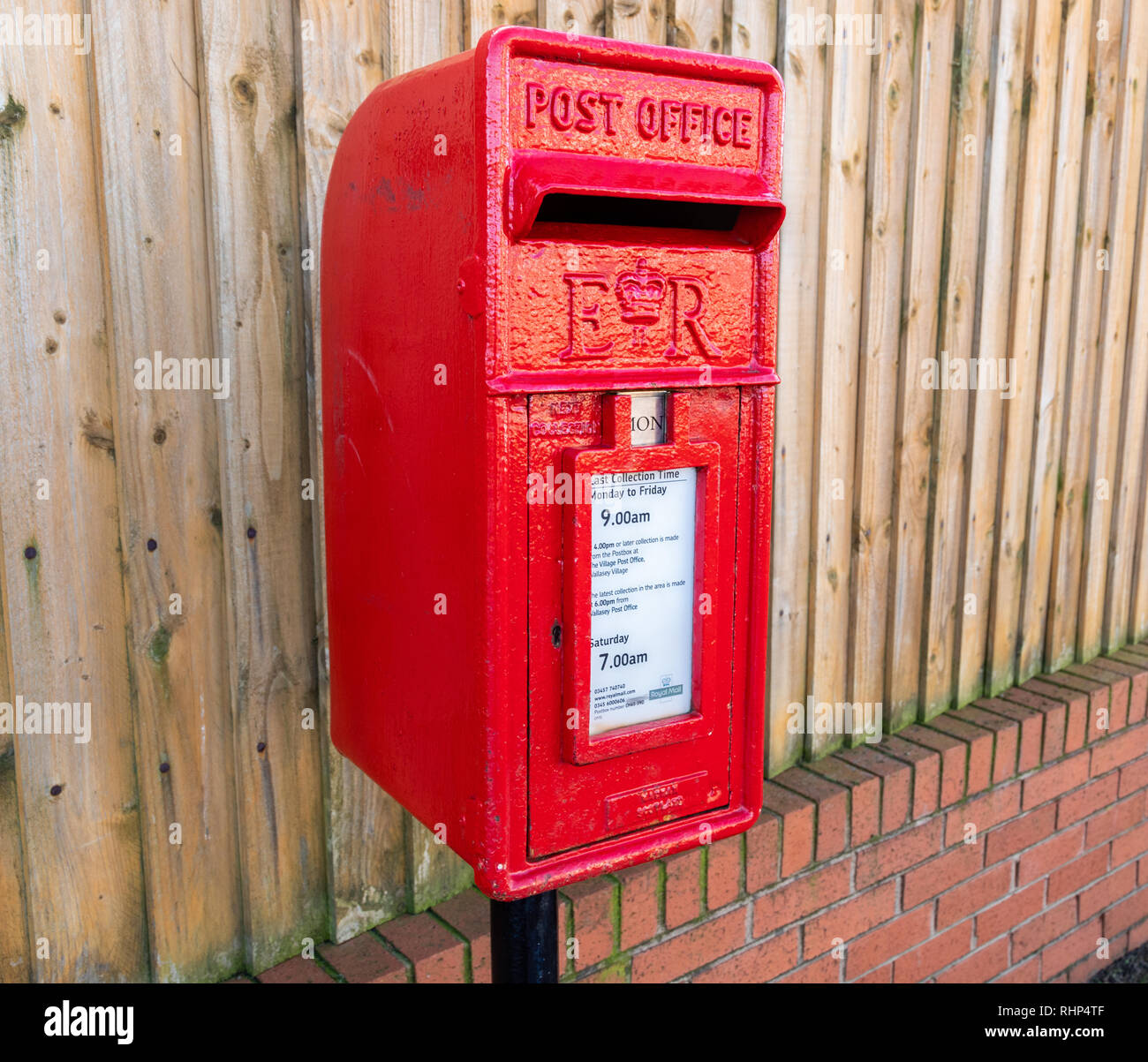 red polemounted post box showing collection times by a wooden fence ...