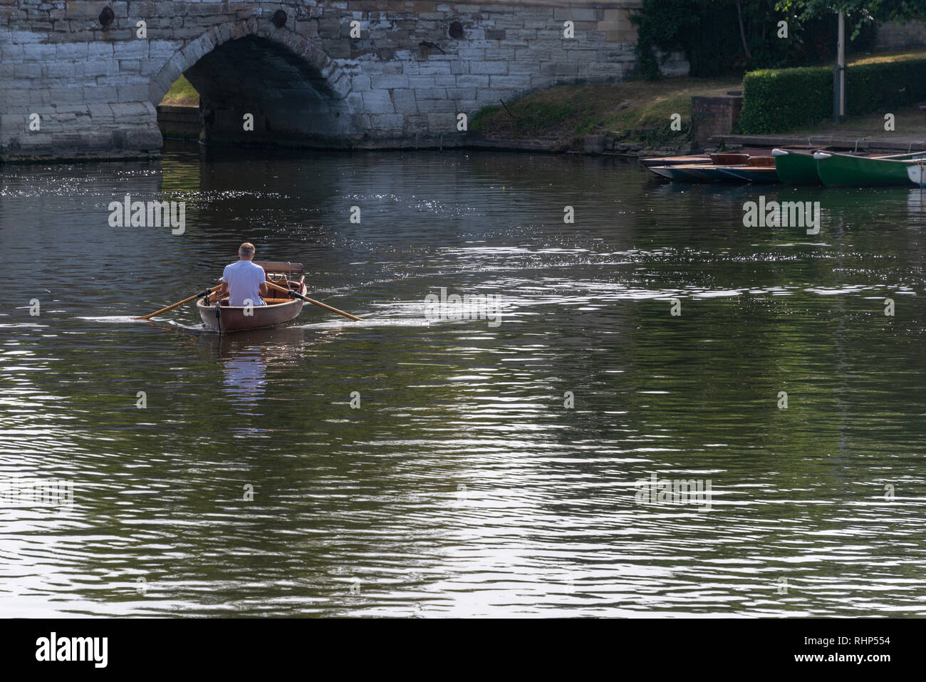 senior man rows boat with ancient stone bridge arch in the background ...