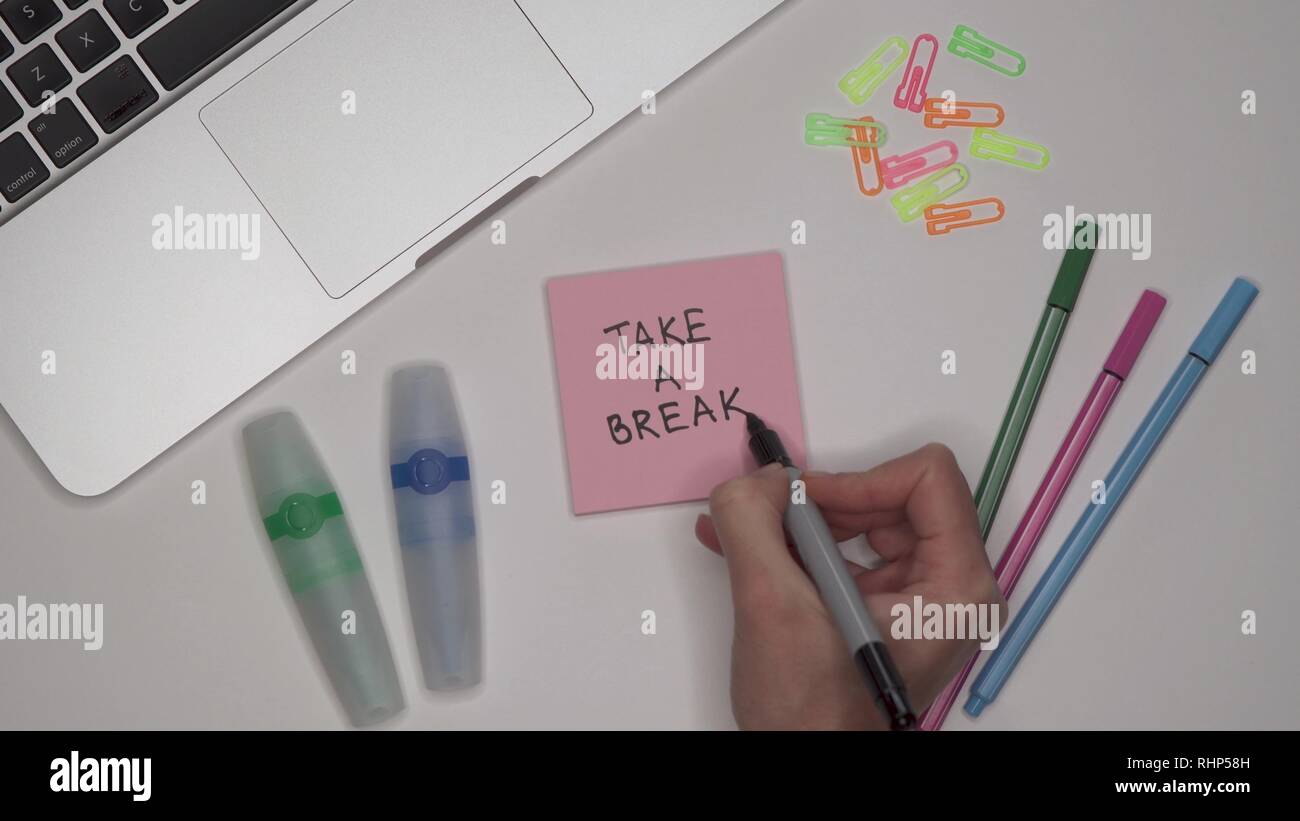 TAKE A BREAK. Woman writing on notepad. Laptop and stationery on the ...