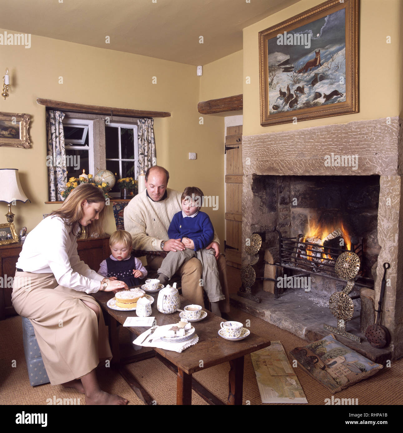 Family having tea beside the fire in country sitting room EDITORIAL USE ...