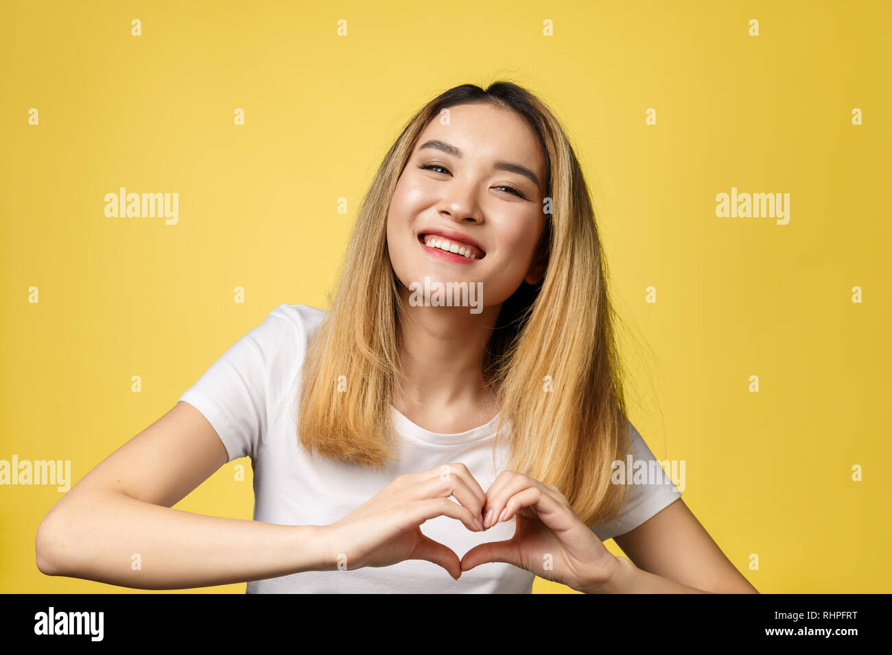 Young Asian woman show heart hand sign isolated on yellow background ...