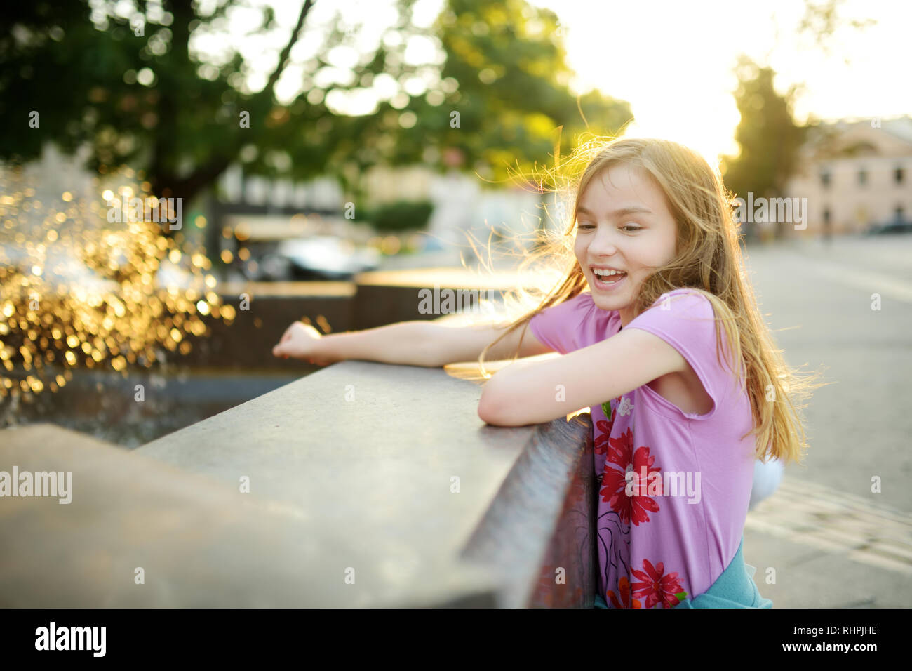 Cute little girl playing by city fountain on hot and sunny summer day ...