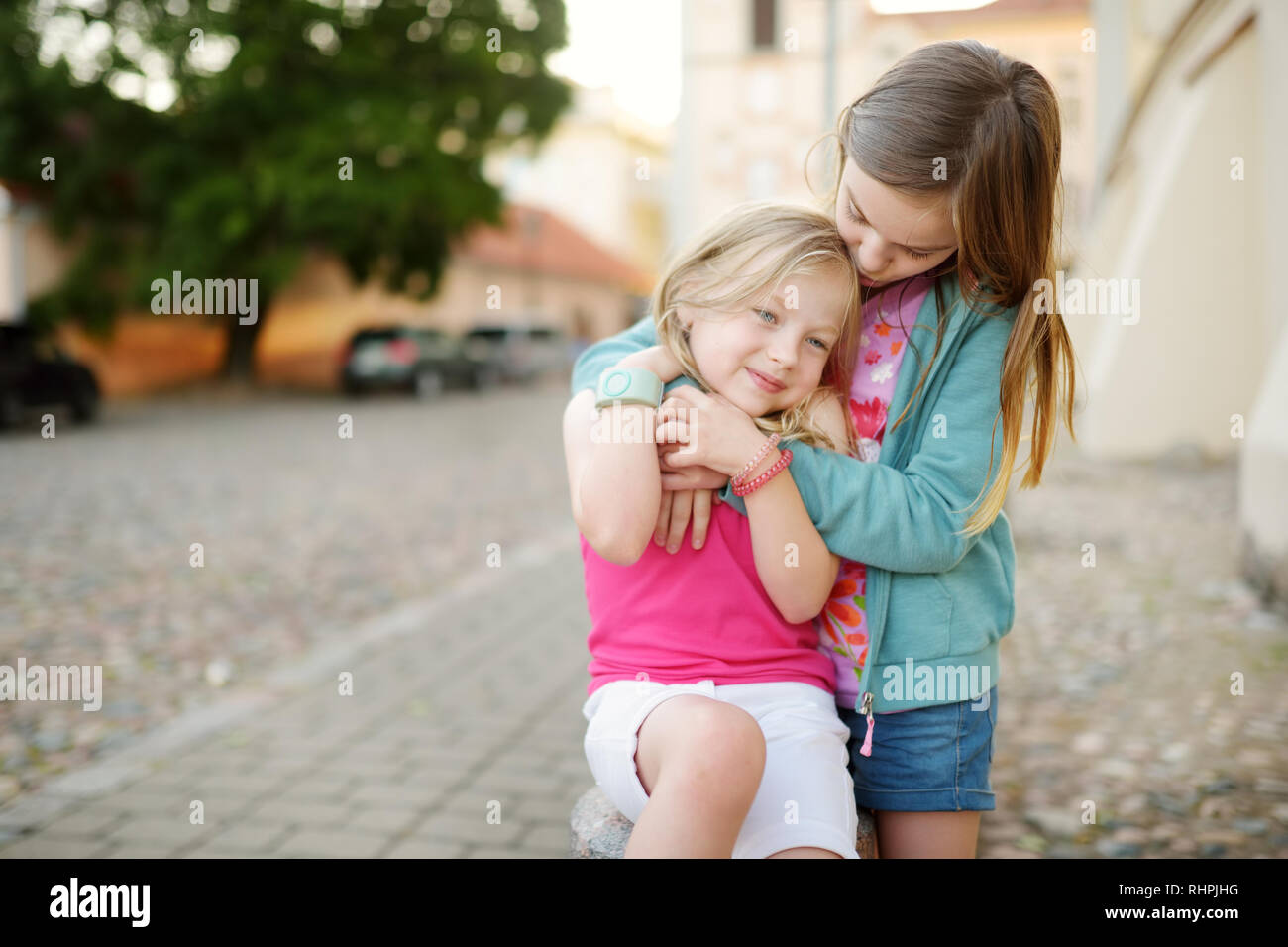 Two adorable sisters laughing and hugging on warm and sunny summer day ...