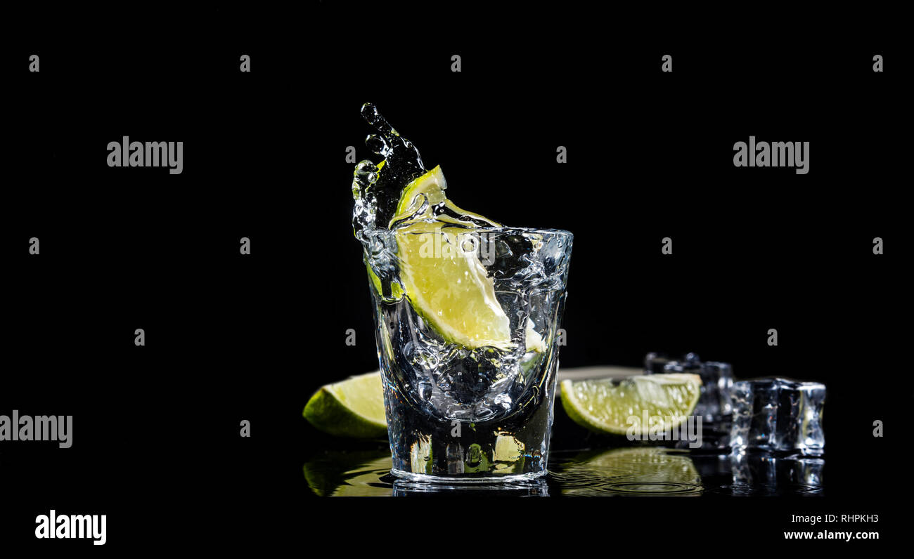 Mexican traditional Tequila splash lime on black background with ice ...