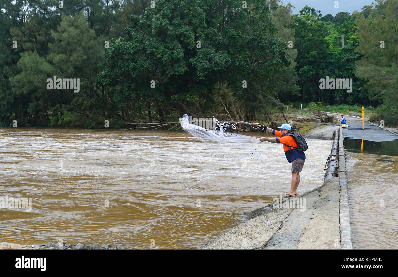 Young man net fishing in the eddies from a flooded bridge over the ...