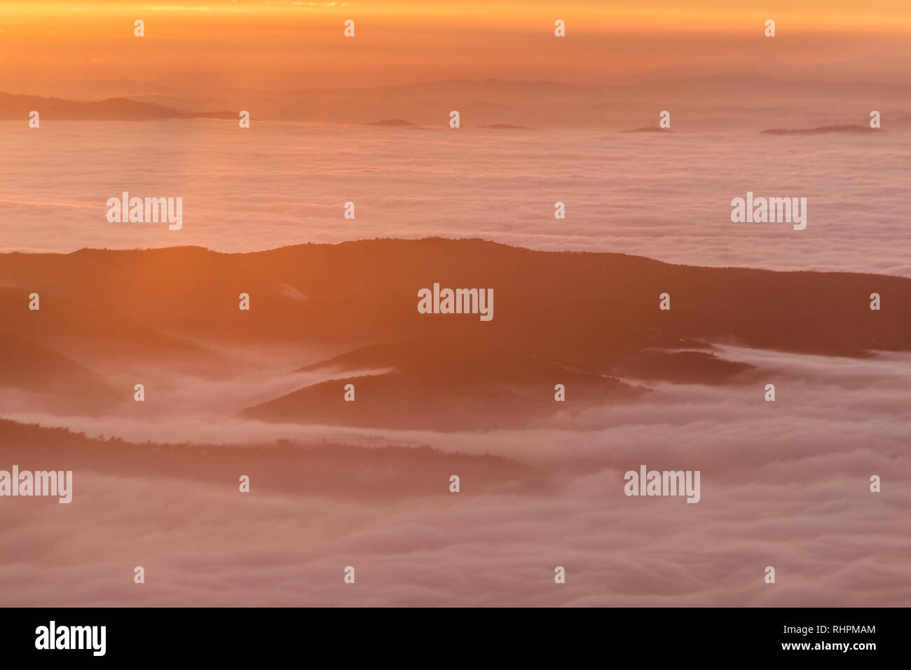 Beautiful sunset over a valley filled by fog with mountains and hills ...