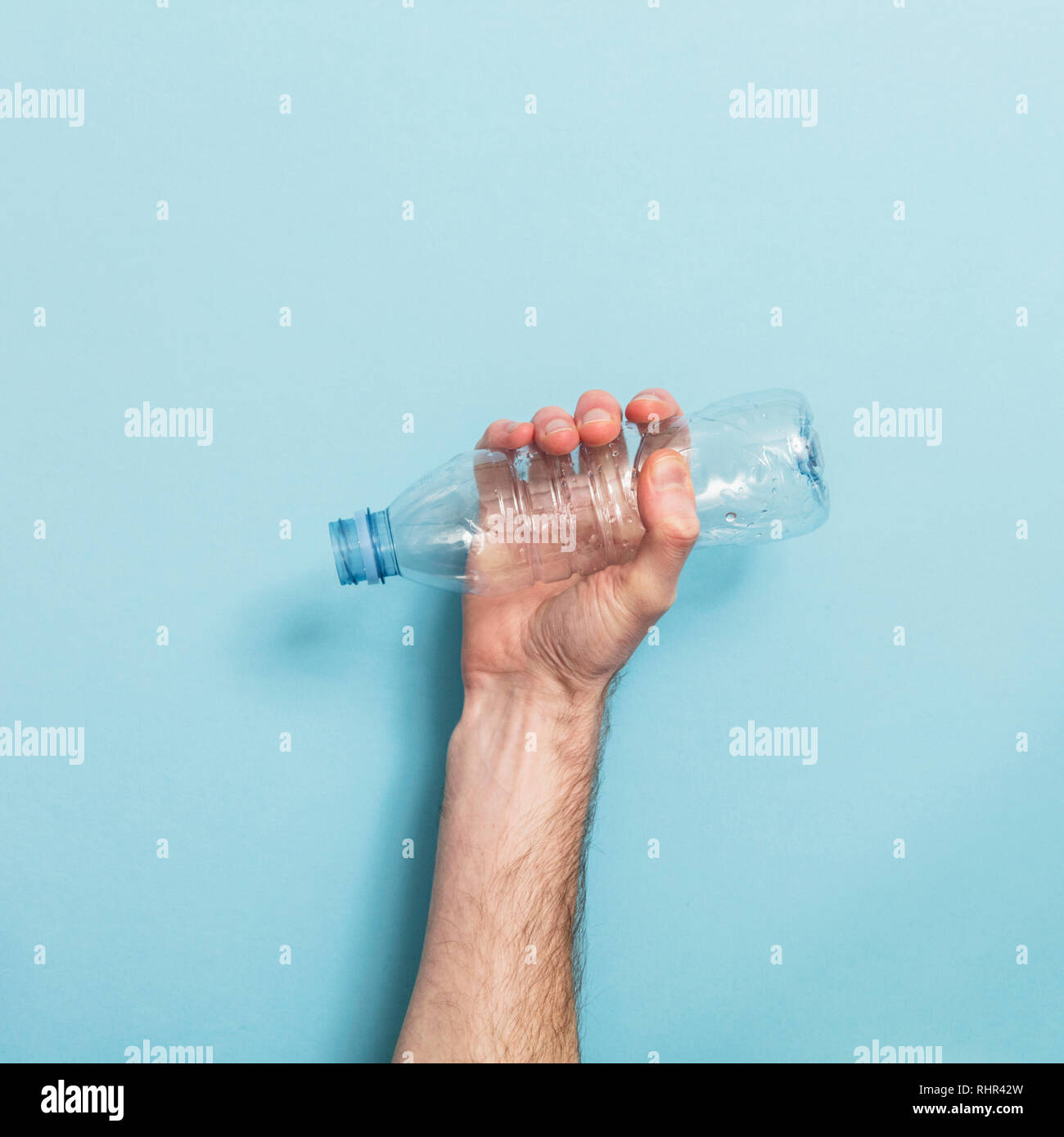Hand holding empty plastic bottle recycling against a blue background ...
