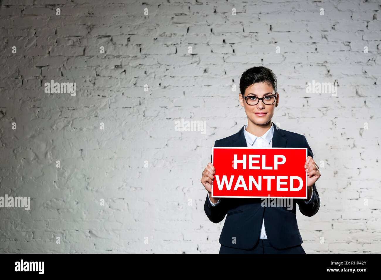 Portrait of beautiful young businesswoman holding help wanted sign ...