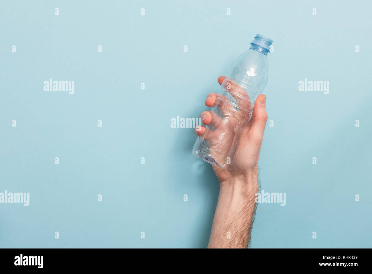Hand holding empty plastic bottle recycling against a blue background ...