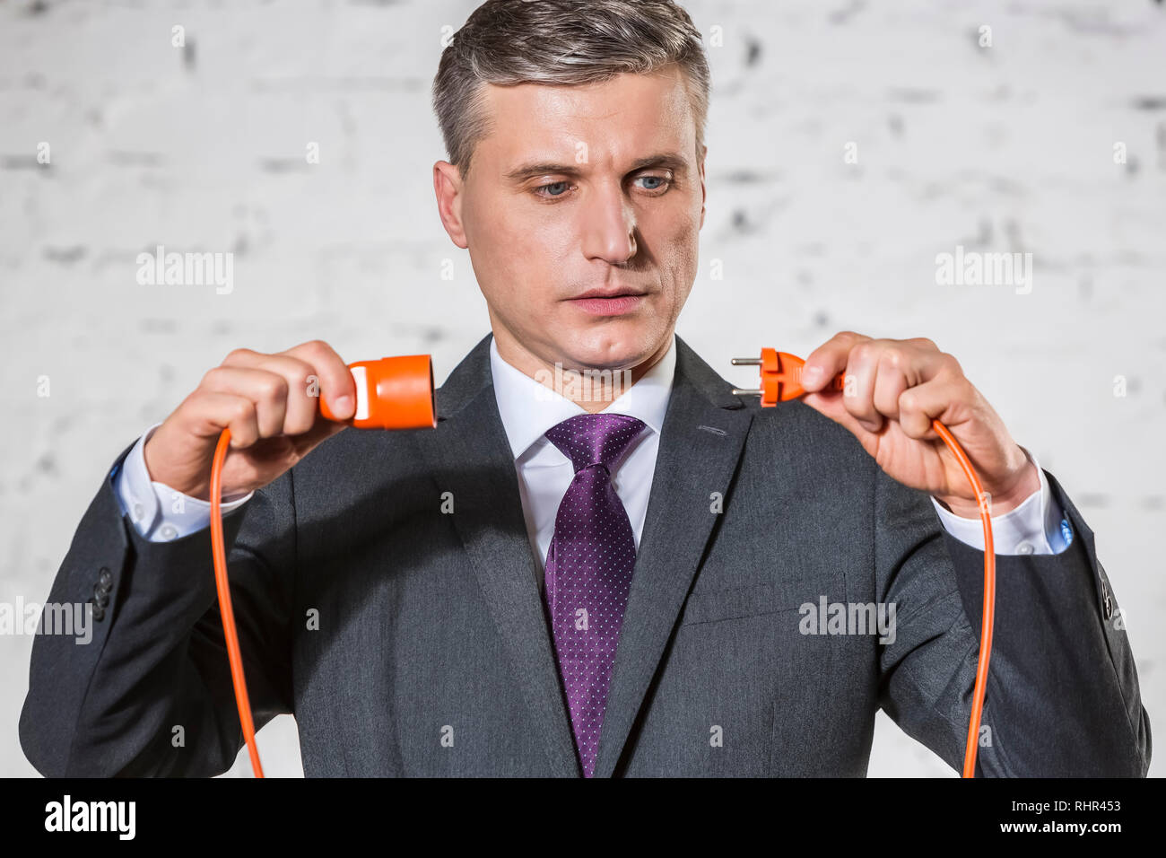 Confident mature businessman attaching red cables against white brick ...