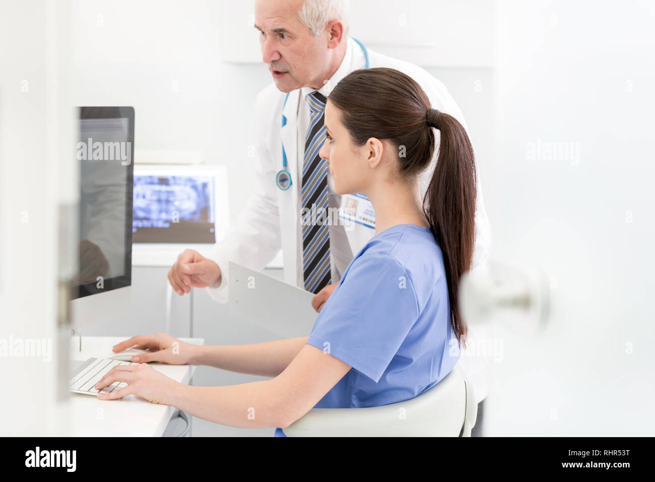 Nurse using laptop at desk while senior doctor explaining in clinic ...