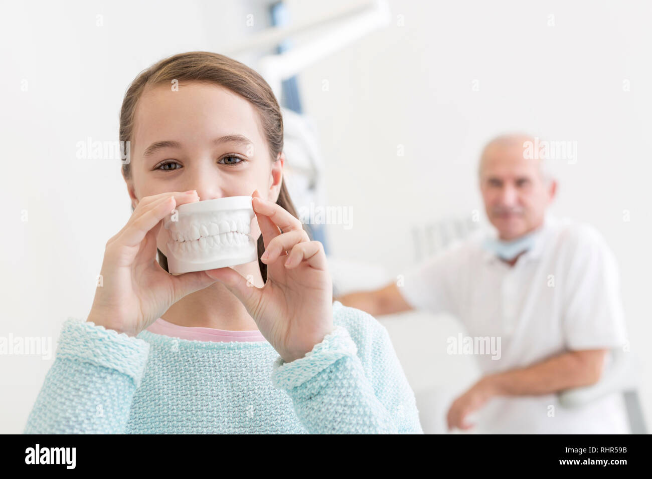 Portrait of girl showing dentures against dentist sitting in dental ...
