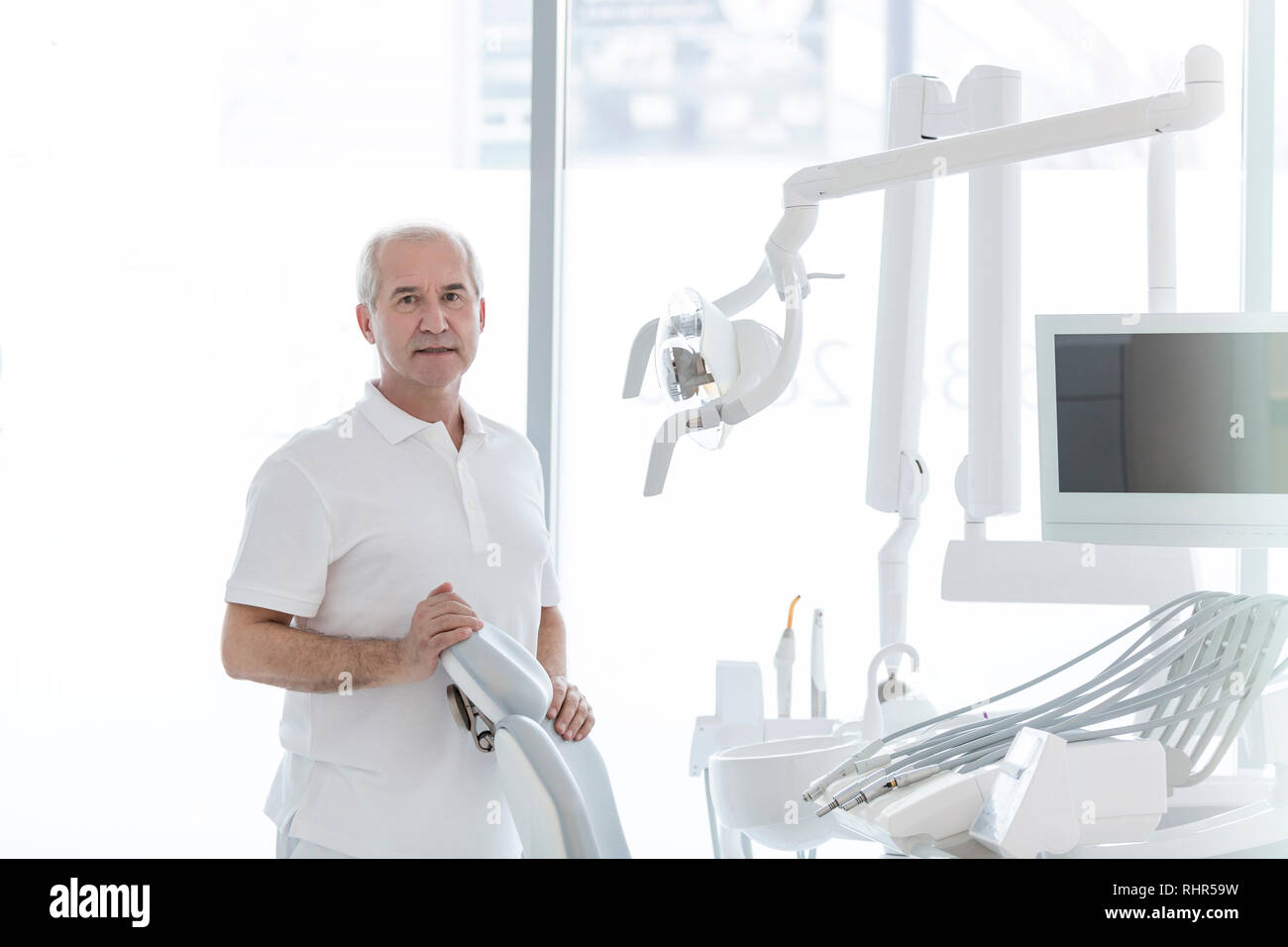 Portrait of senior dentist standing by chair at dental clinic Stock ...