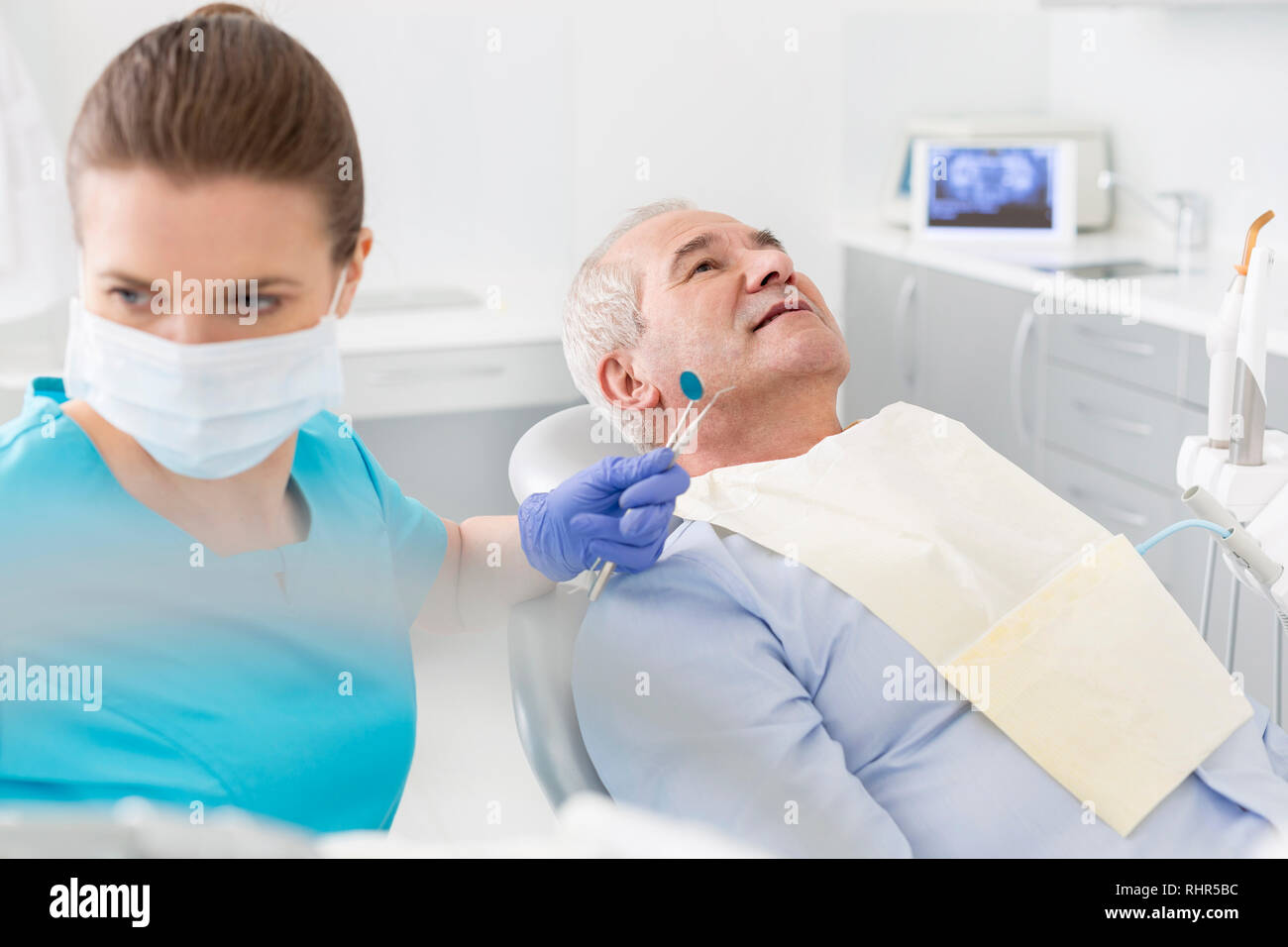 Mid adult dentist with equipment treating senior patient at clinic ...