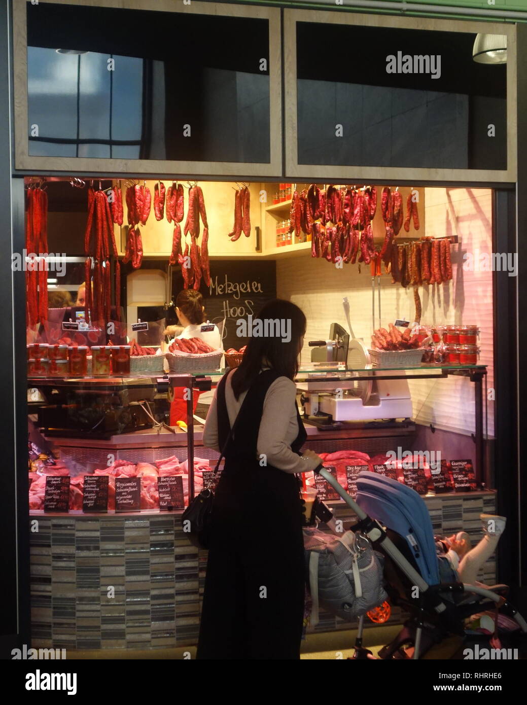 A lady with a pram buying meat from a butchers stall at Kleinmarkthalle ...