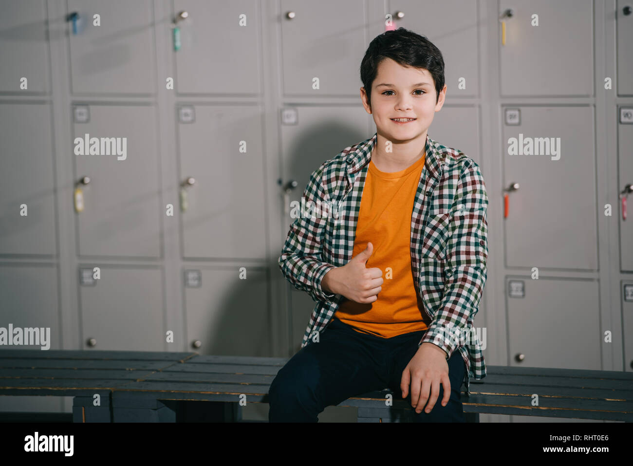 Smiling brunette kid showing thumb up while posing in locker room Stock ...