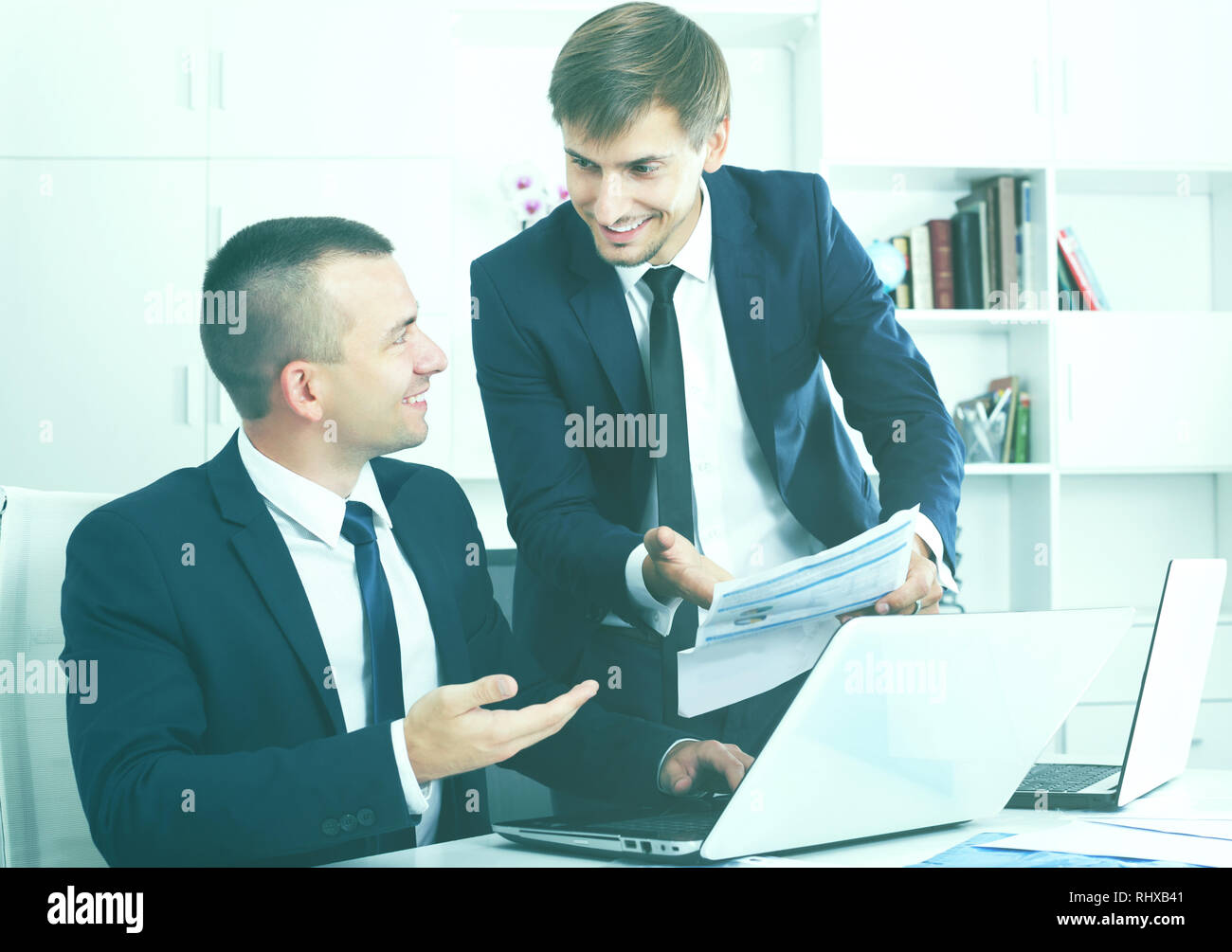 Two young smiling business men colleagues working together with laptops ...