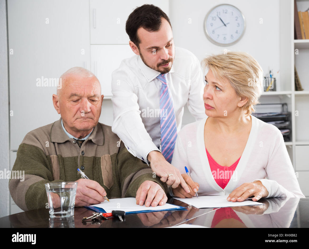 Old husband and wife signing agreement papers in bank with manager ...