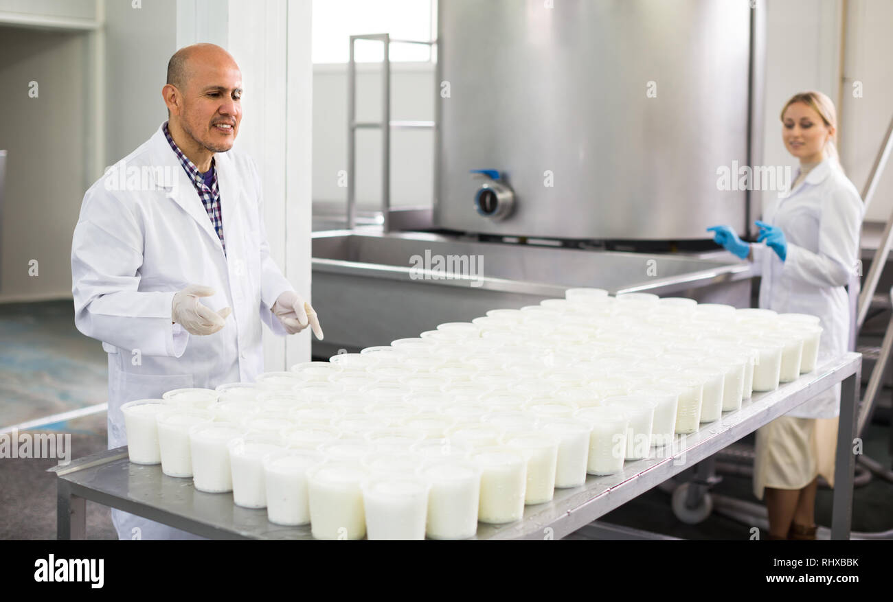 Smiling man and woman wearing uniform working on cottage cheese ...