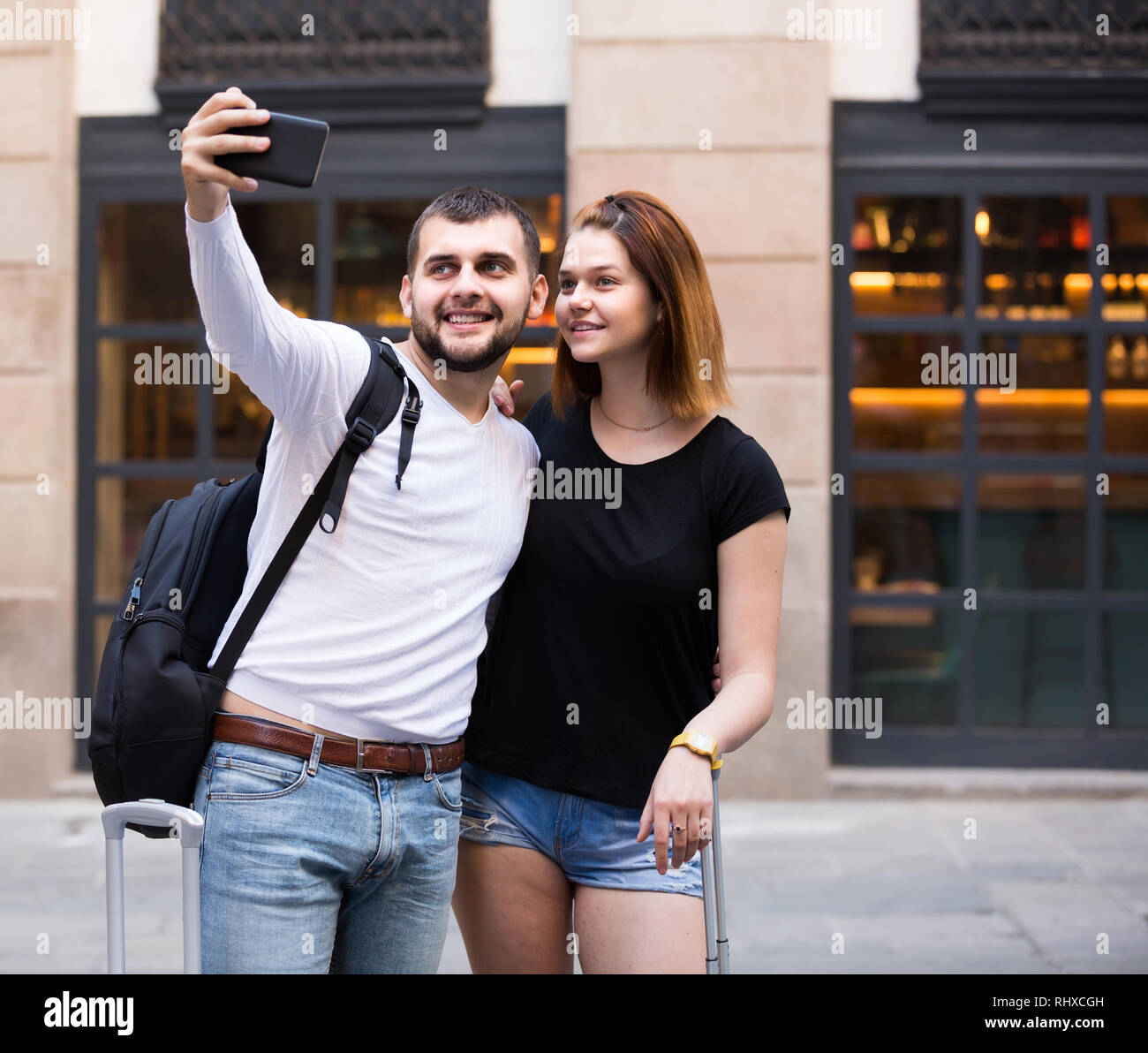 Smiling spanish female and male standing with baggage at street and ...