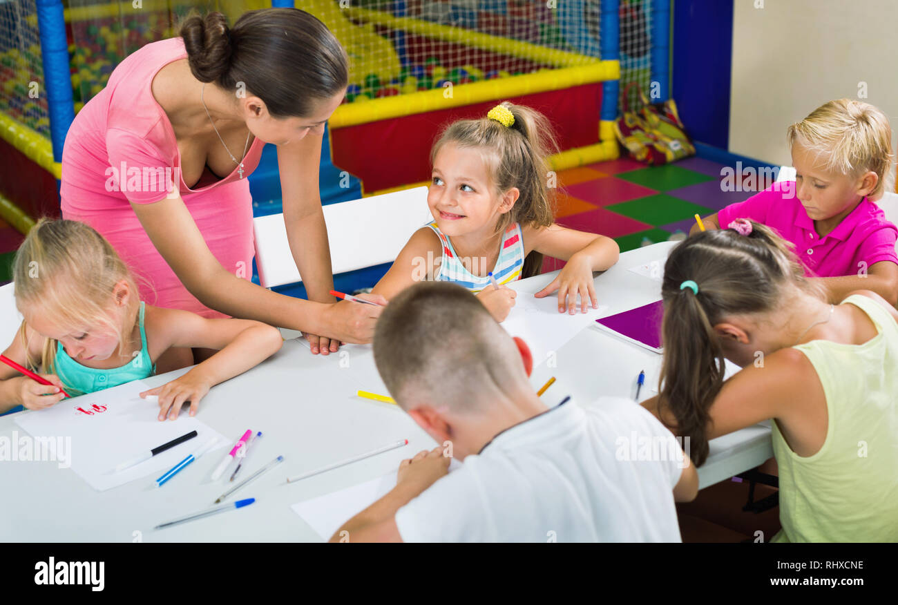 Smiling happy diligent kids drawing together with tutor at hobby group ...