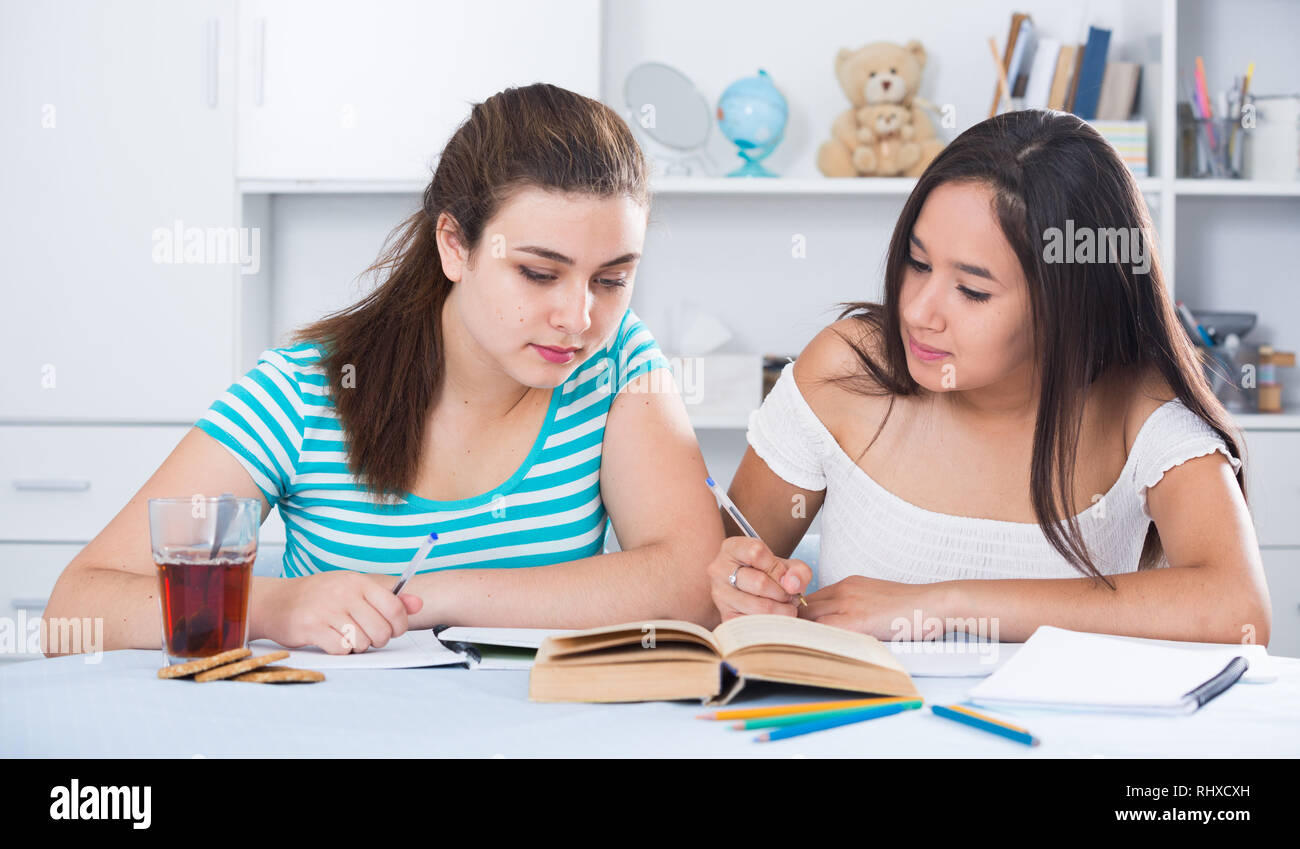 Teenagers girls studying with textbook at table at home and helping ...
