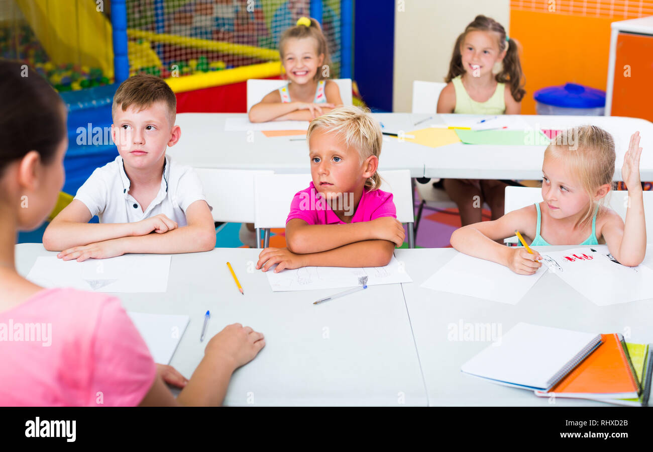 primary school kids sitting at the desks and attentively listening to a ...