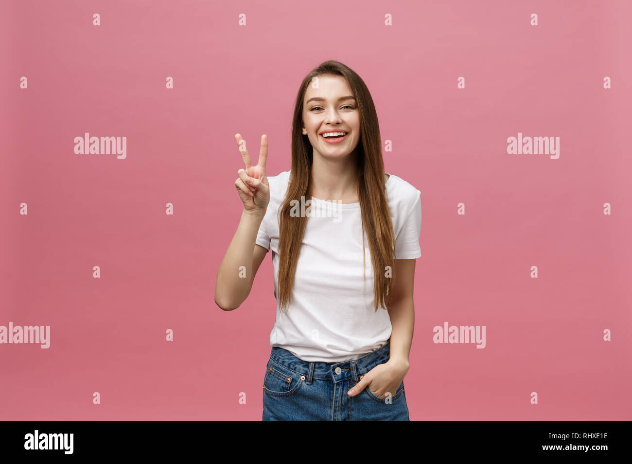 Portrait of a cheerful trendy woman showing two fingers sign over pink ...