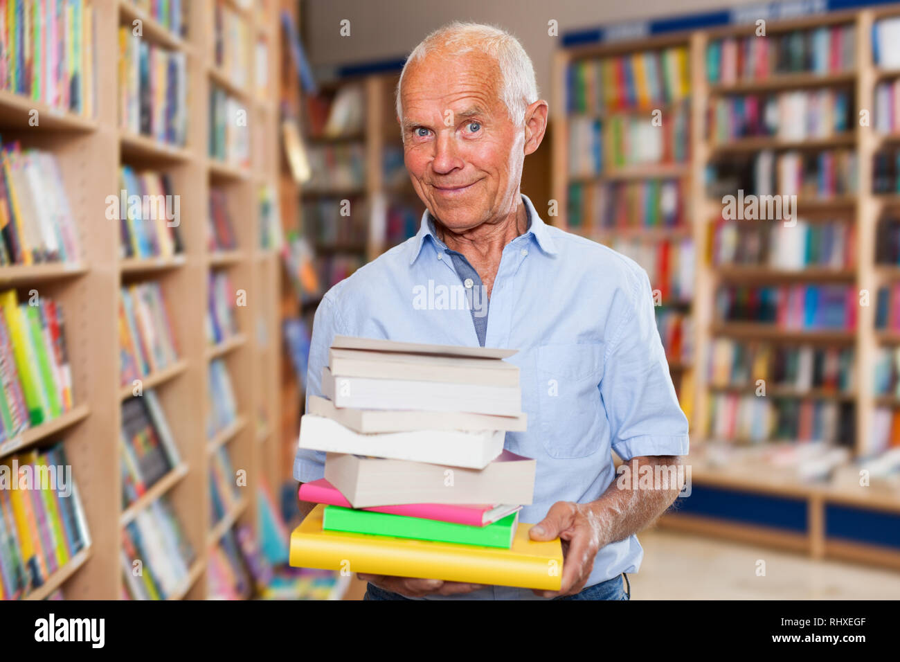 Portrait of charismatic older man standing in library with pile of ...