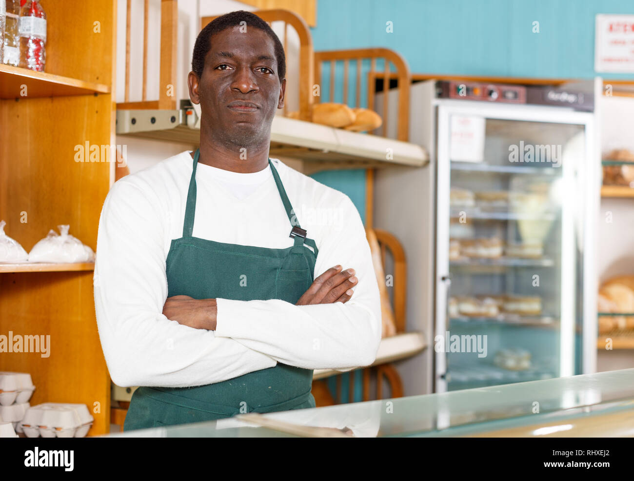 Proud owner of bakery shop standing with arms folded behind counter ...