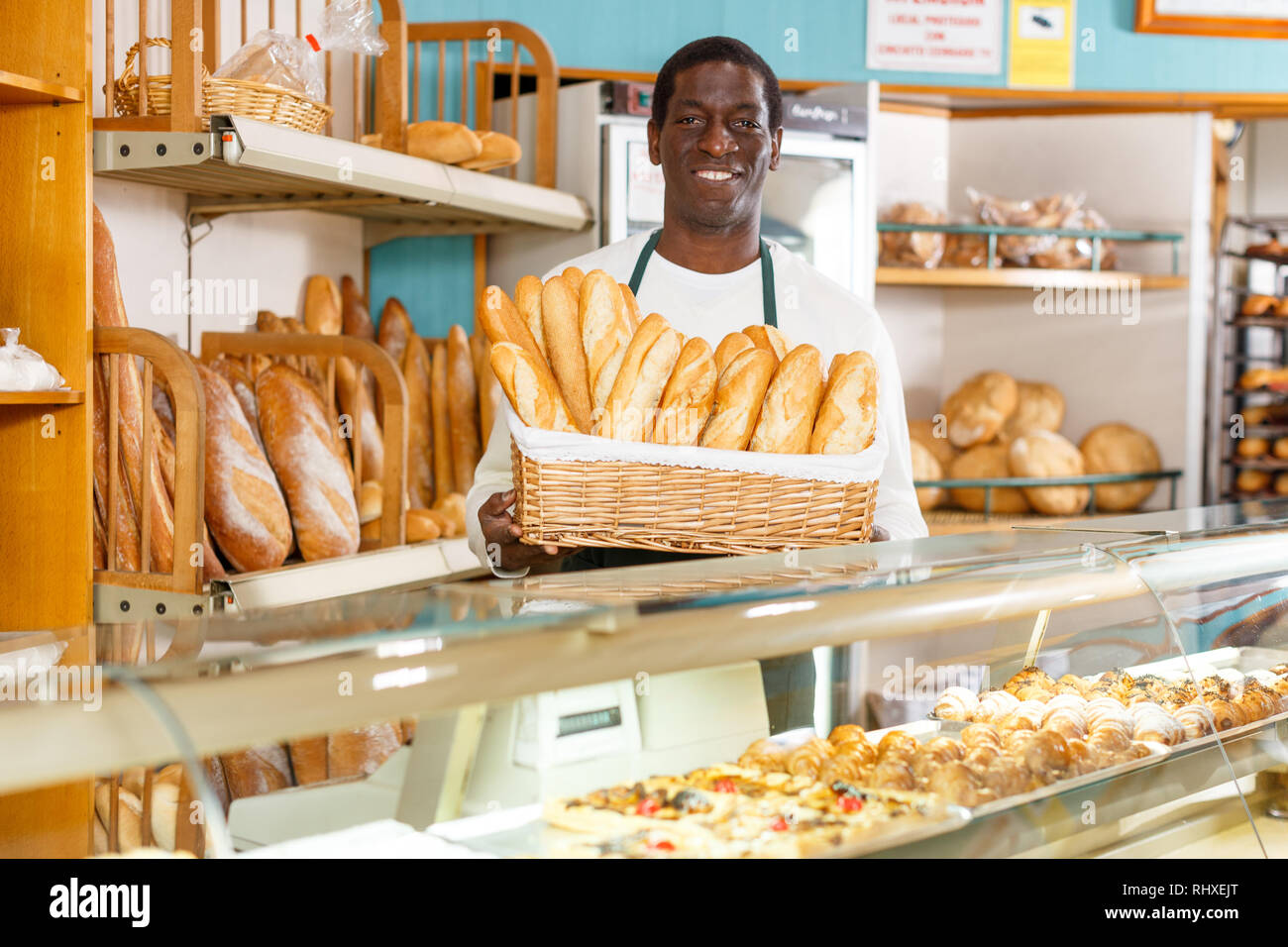 Happy bakery seller holding wicker basket with fresh bread in shop of ...
