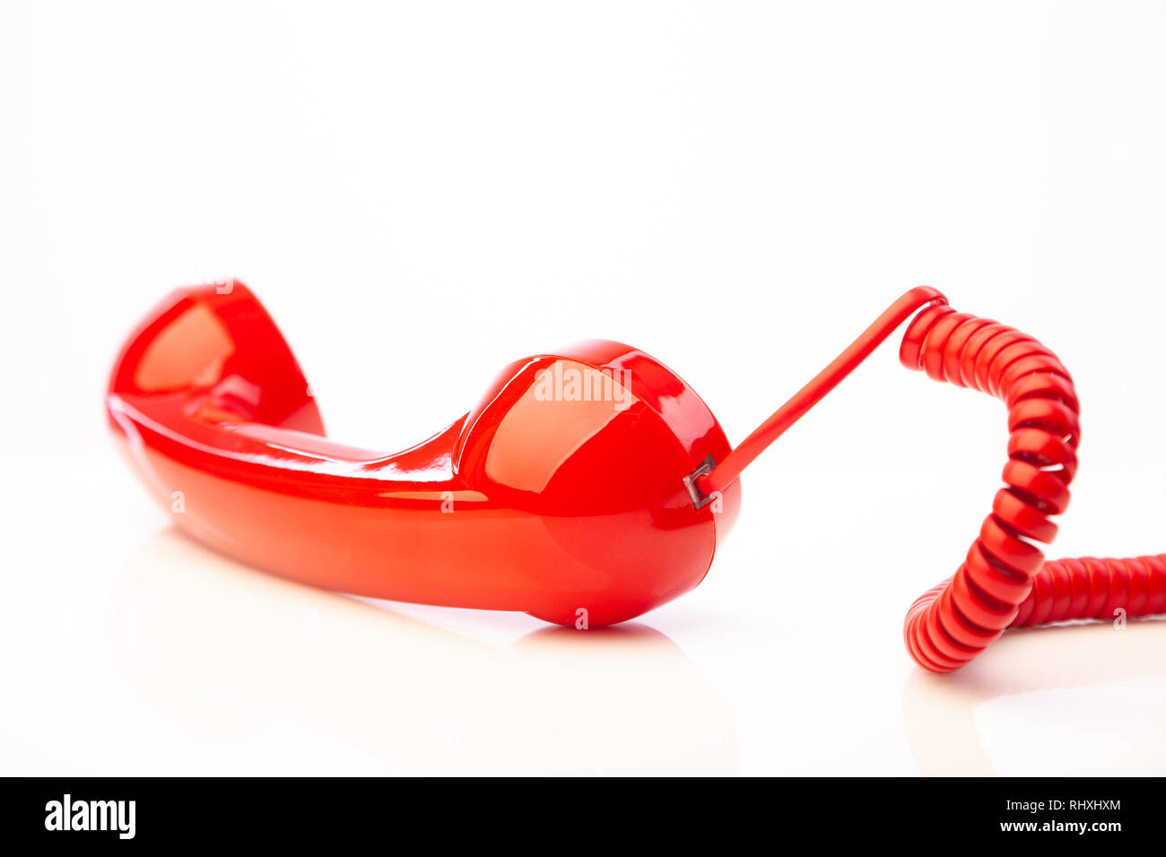 A red retro telephone handset lying on it's side against a white ...