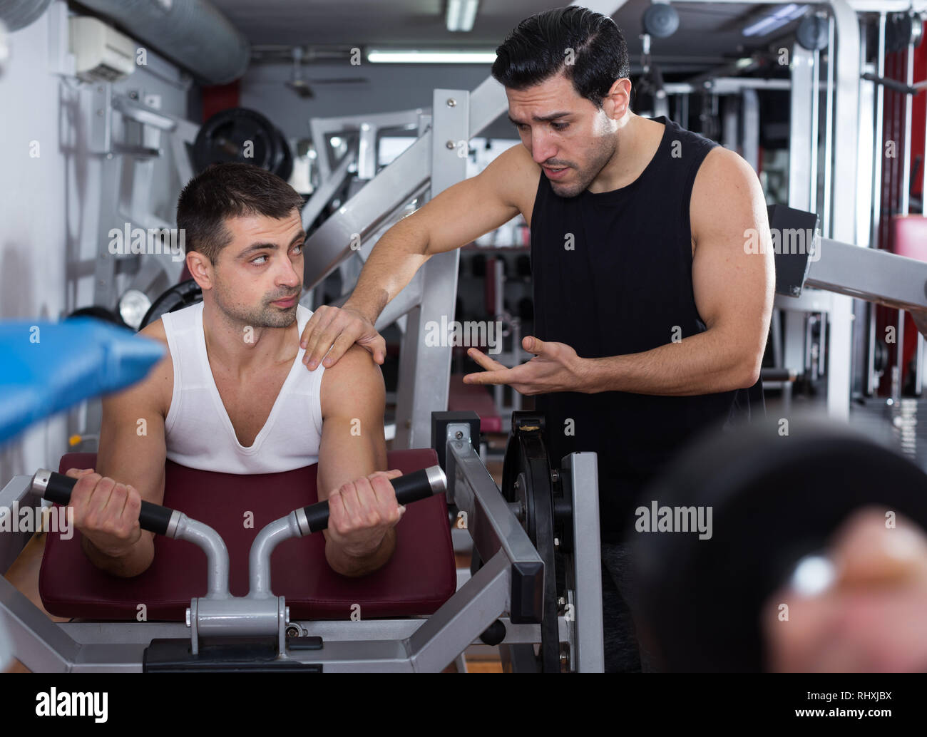 Male trainer explaining to muscular guy technique of performing ...
