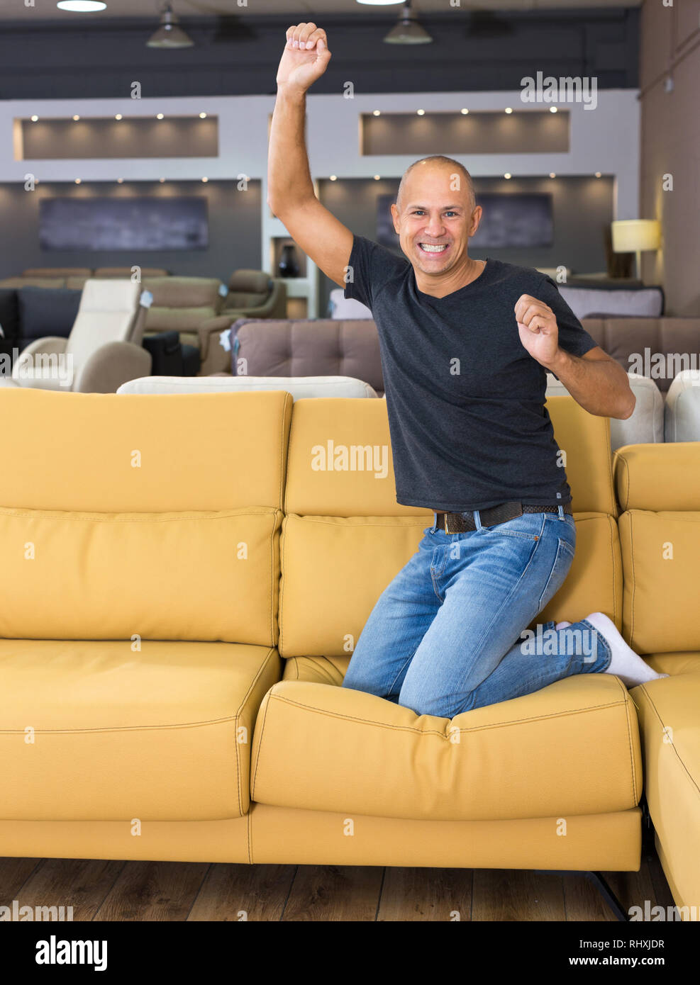 Funny happy man jumping on yellow couch in furniture shop Stock Photo ...