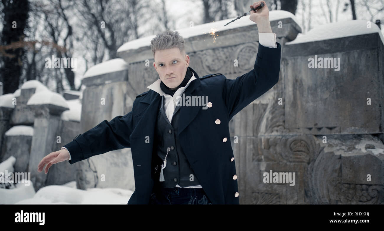 Young man in image of black magician makes a spell using magic wand ...