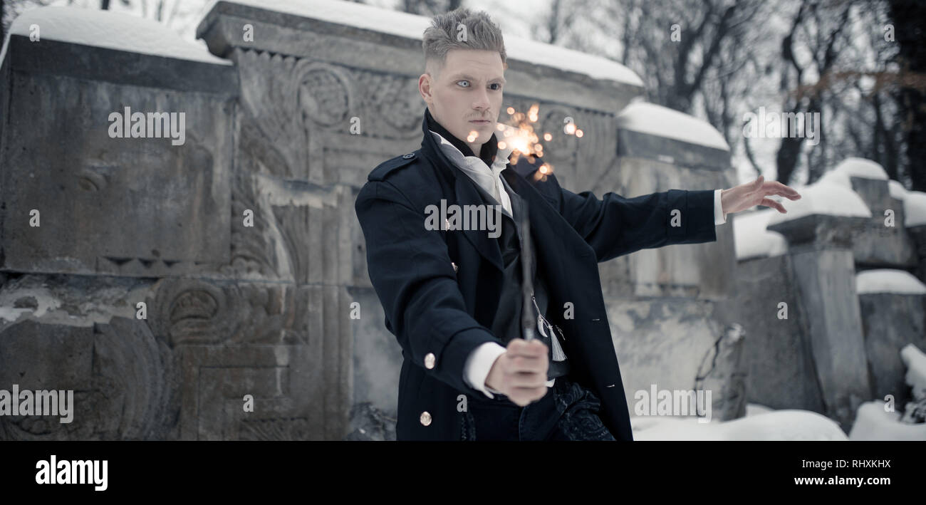 Young man in image of black magician makes a spell using magic wand ...